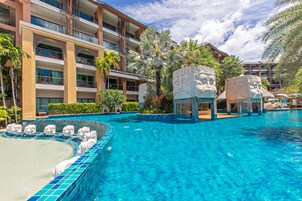 Resort com uma piscina grande, palmeiras e um edifício com varandas.