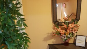 Um corredor com sinal de SAÍDA, um espelho, um vaso com flores e uma placa emoldurada sobre uma mesa.