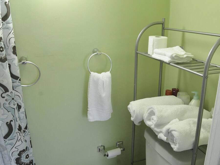 Um banheiro pequeno com vaso sanitário, cortina de chuveiro, porta-toalhas e prateleira com toalhas e artigos de higiene pessoal.