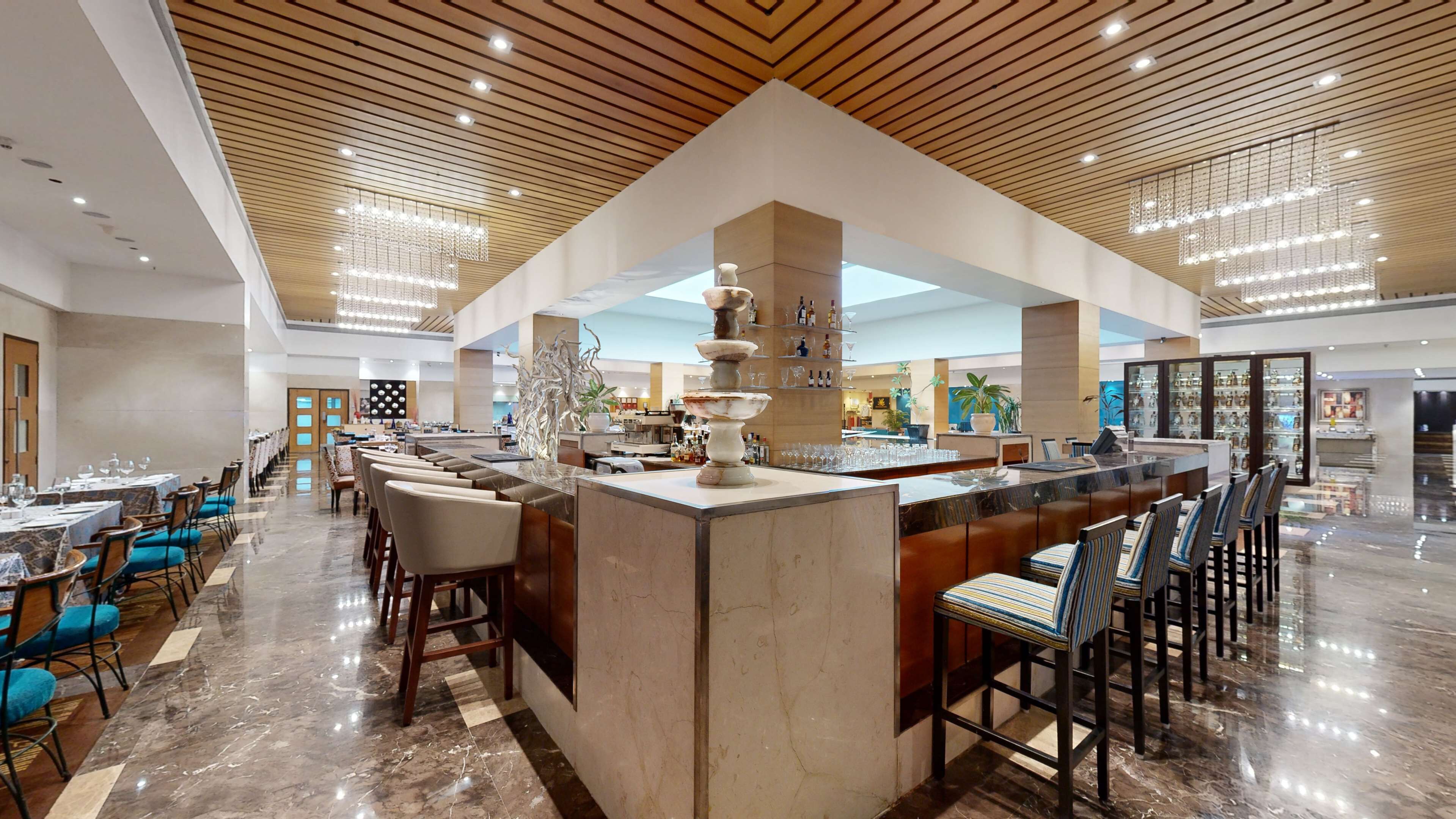 Um hall de hotel espaçoso com um bar central, diversas opções de assento e um lustre moderno.