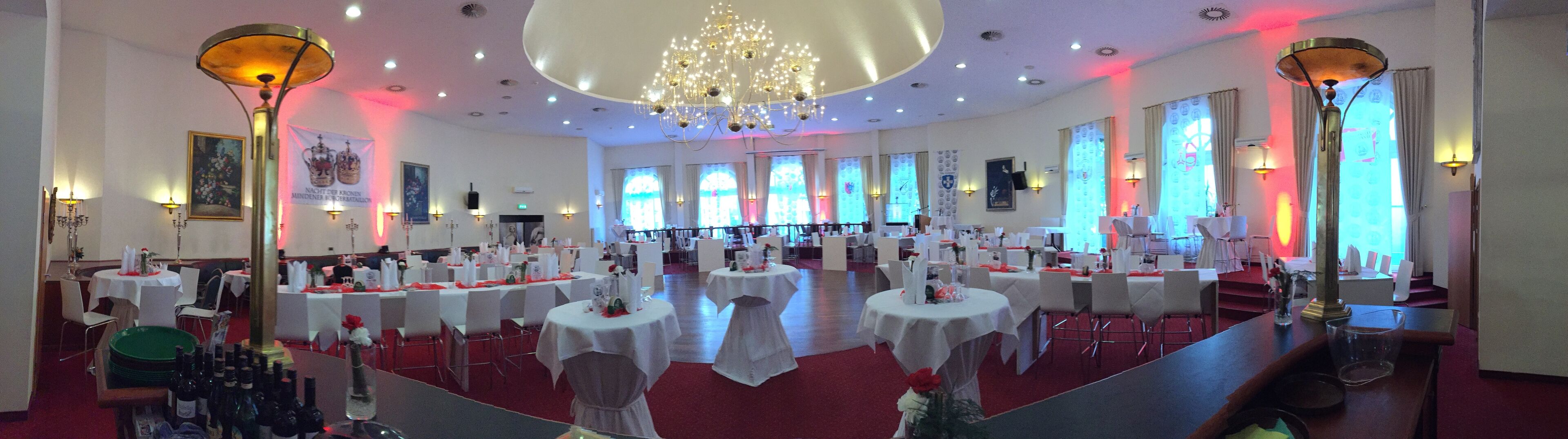 Uma sala de banquetes com mesas redondas, toalhas brancas e tapetes vermelhos.