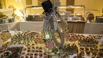 Mesa de buffet com diversos alimentos e uma peça central decorativa em formato de árvore de prata.