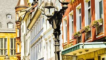Rua com edifícios históricos, mesas ao ar livre e um poste de luz.