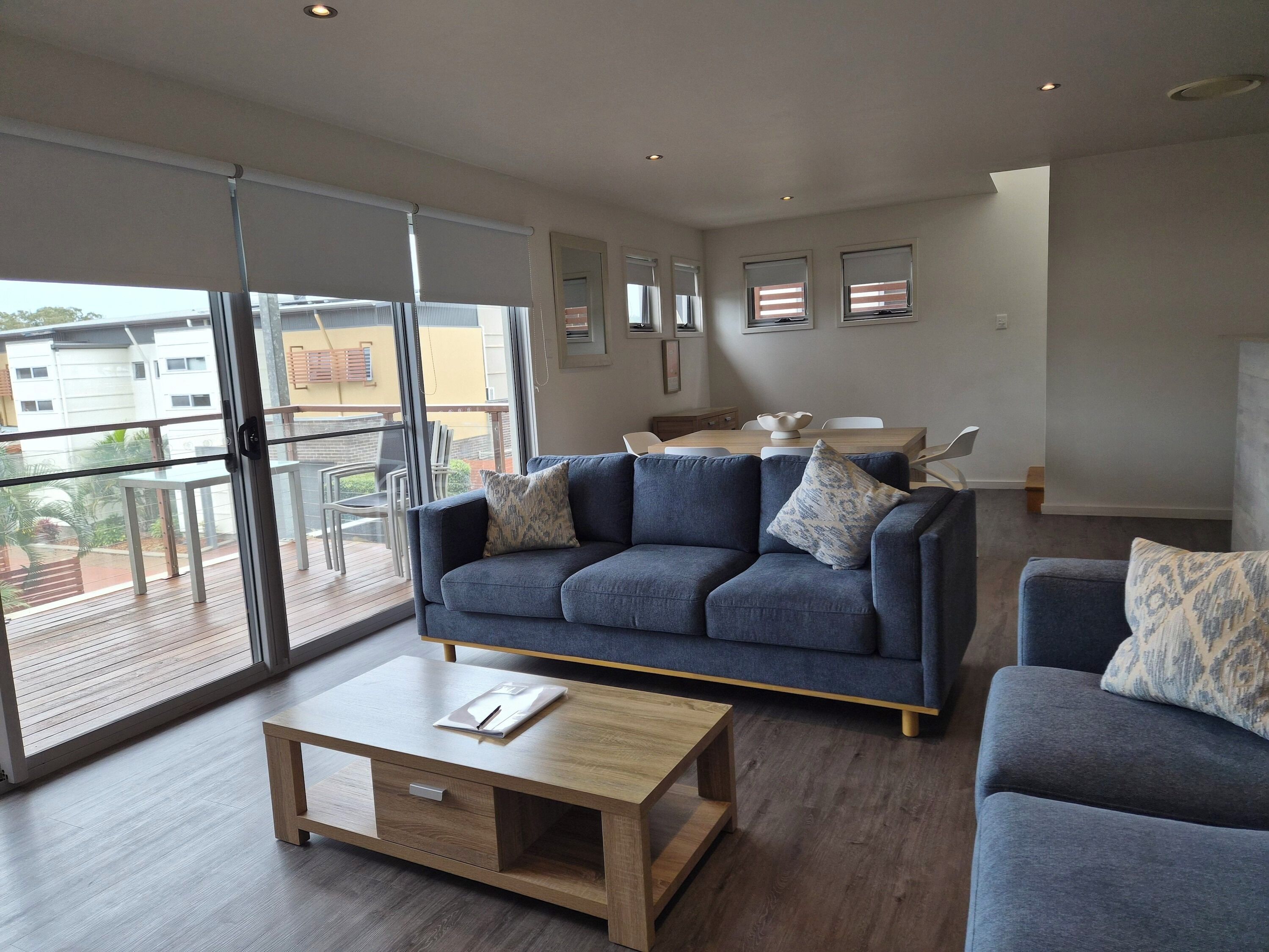 Uma sala de estar moderna com um sofá azul, uma mesa de centro de madeira e uma área de jantar com uma mesa e cadeiras brancas.