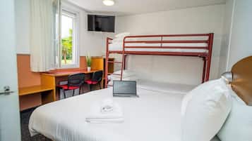 Quarto de hotel com beliche, escrivaninha com cadeira, laptop e televisão na parede.