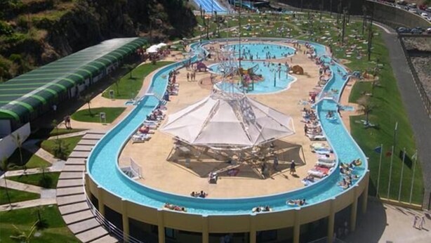 Um complexo amplo e circular de piscinas, com várias áreas e um pavilhão central.