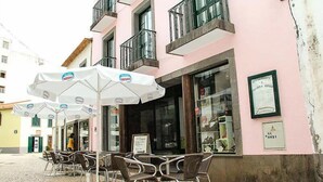 Mesas ao ar livre com guarda-sóis, um prédio rosa e uma placa.