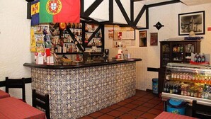 Uma área de bar com balcão revestido de azulejos, prateleiras com garrafas e uma bandeira.