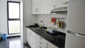 Cozinha com armários brancos, bancada preta, pia e geladeira.