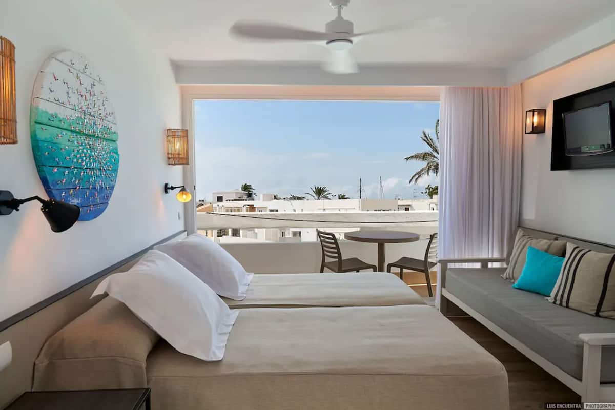 Quarto de hotel com varanda, ventoinha no teto, televisão e vista para a cidade.