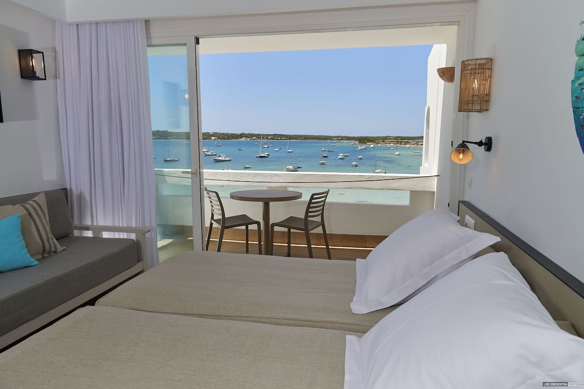 Quarto de hotel com varanda, sofá, cama, mesa e cadeiras.