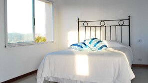 Uma cama de solteiro com cabeceira de metal, roupa de cama branca e travesseiro listrado.