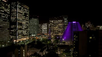 Paisagem urbana noturna com arranha-céus iluminados e um edifício em formato de pirâmide com iluminação roxa.