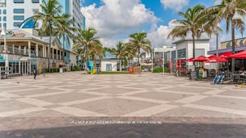 Uma praça ampla e pública com palmeiras, piso xadrez e diversas lojas.