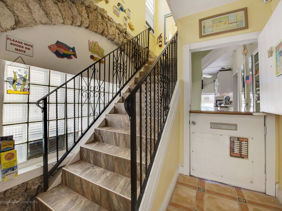 Uma escadaria com corrimãos pretos leva a um patamar com uma porta branca e uma placa indicando 'CORAL HOUSE HOURS'.