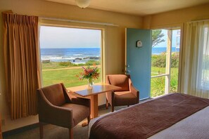 Quarto de hotel com cama, duas cadeiras, uma mesa e vista para o mar.