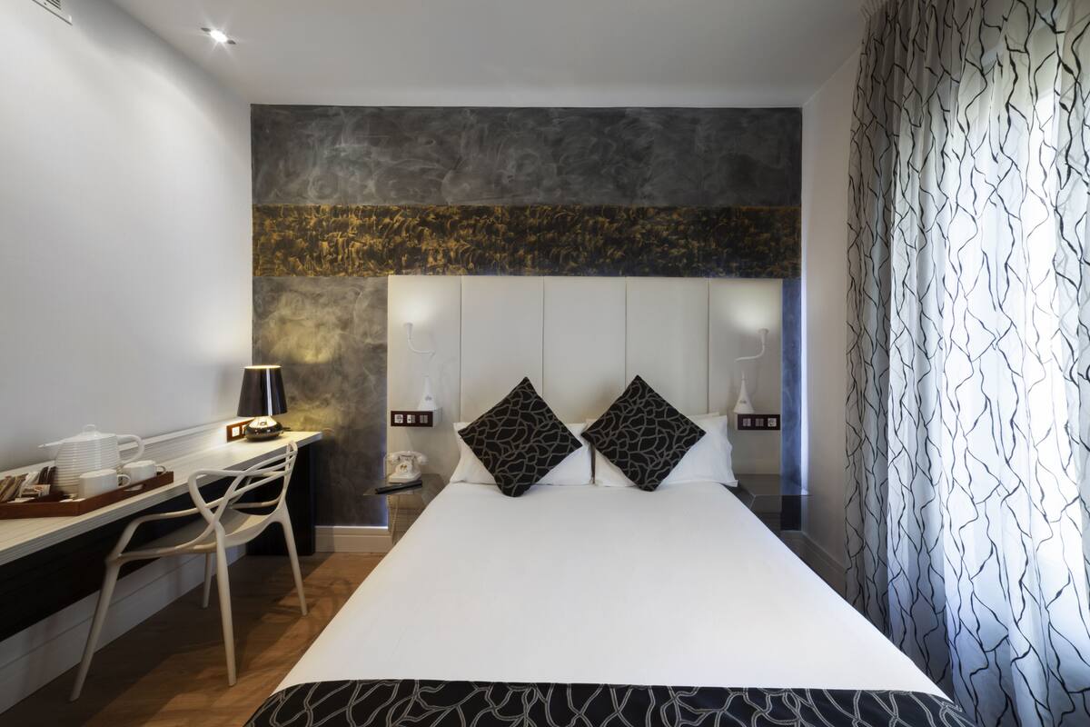 Quarto de hotel moderno com uma cama grande, uma escrivaninha com abajur e uma parede estampada.