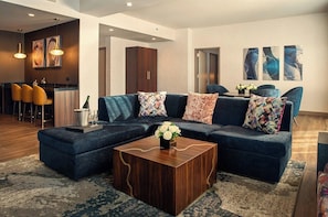 Uma sala de estar moderna com sofá seccional, mesa de centro de madeira e área de bar com banquetas.