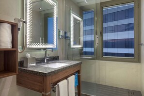 Uma casa de banho moderna com lavatório de bancada de granito, um espelho grande com iluminação e uma janela com persianas.
