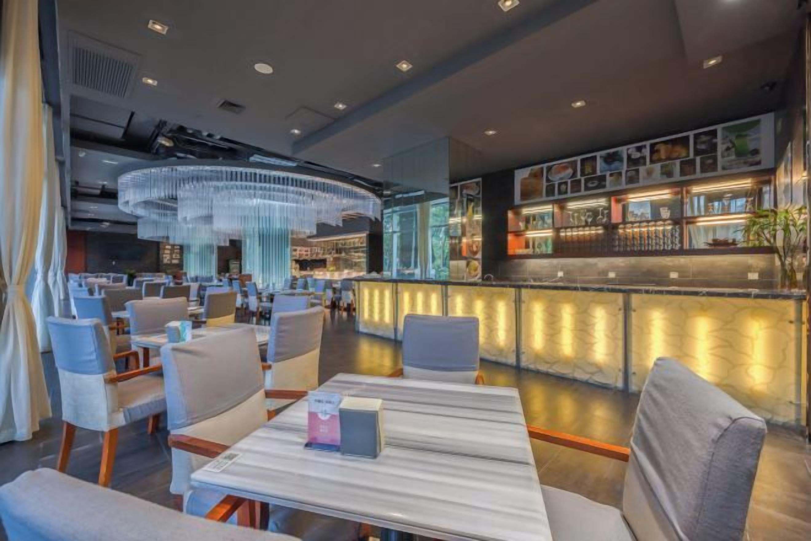 Um restaurante moderno com área de bar, arranjos de assento e um lustre decorativo.