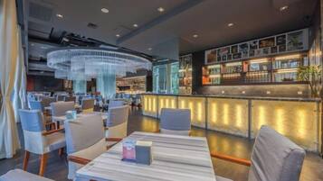 Um restaurante moderno com área de bar, arranjos de assento e um lustre decorativo.