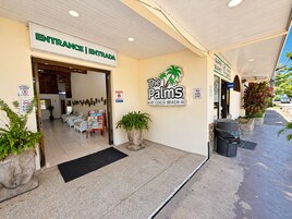 Entrada de hotel com placa indicando 'ENTRANCE | ENTRADA', logotipo de palmeira e sinal de 'VISA'.