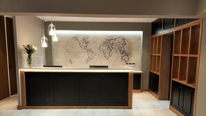 Balcão de recepção com mapa-múndi ao fundo, prateleiras de madeira e iluminação pendente.