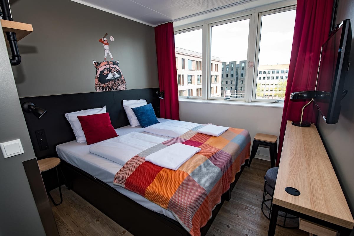 Quarto de hotel moderno com uma cama grande, uma escrivaninha e uma janela com vista para a cidade.