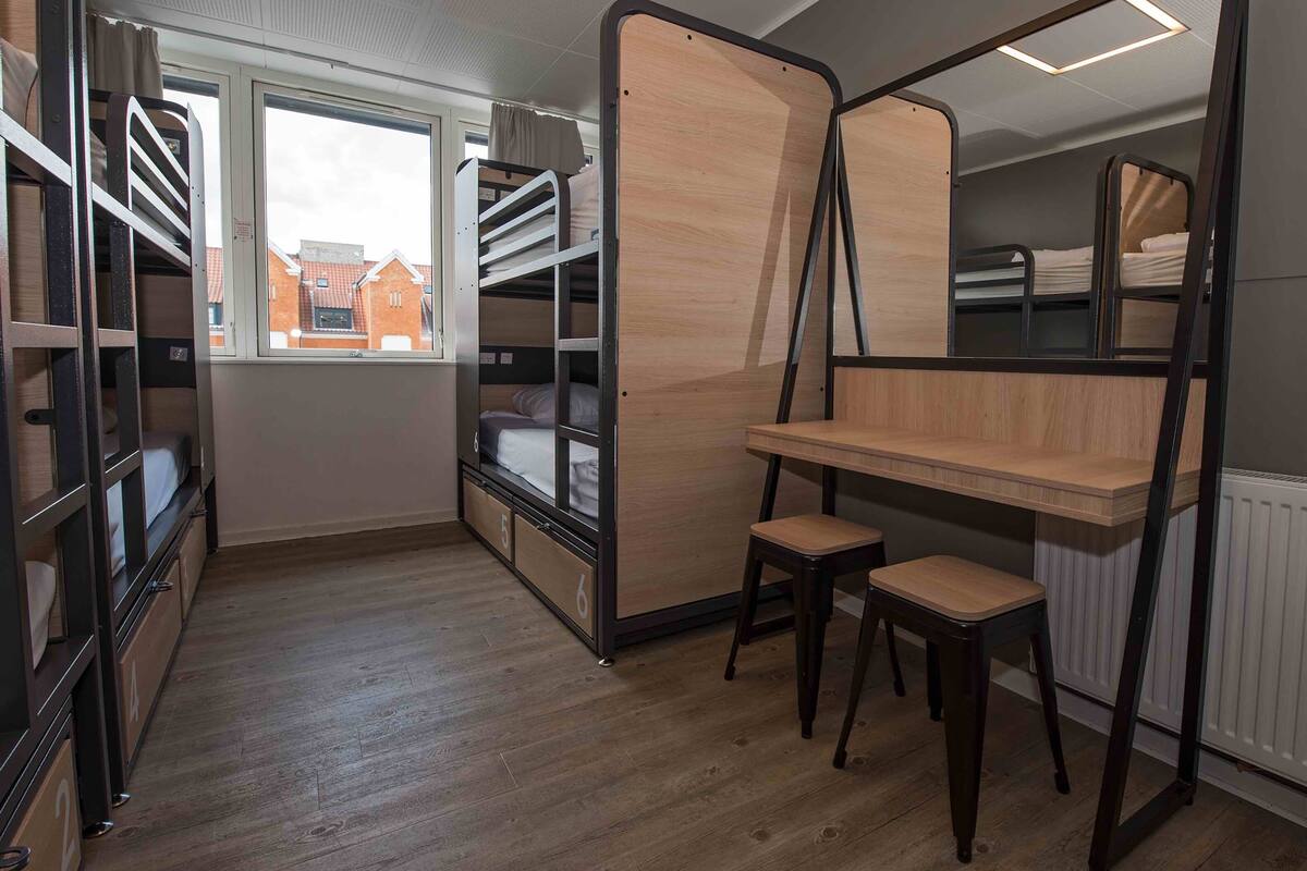 Quarto pequeno com beliche, escrivaninha e espelho.