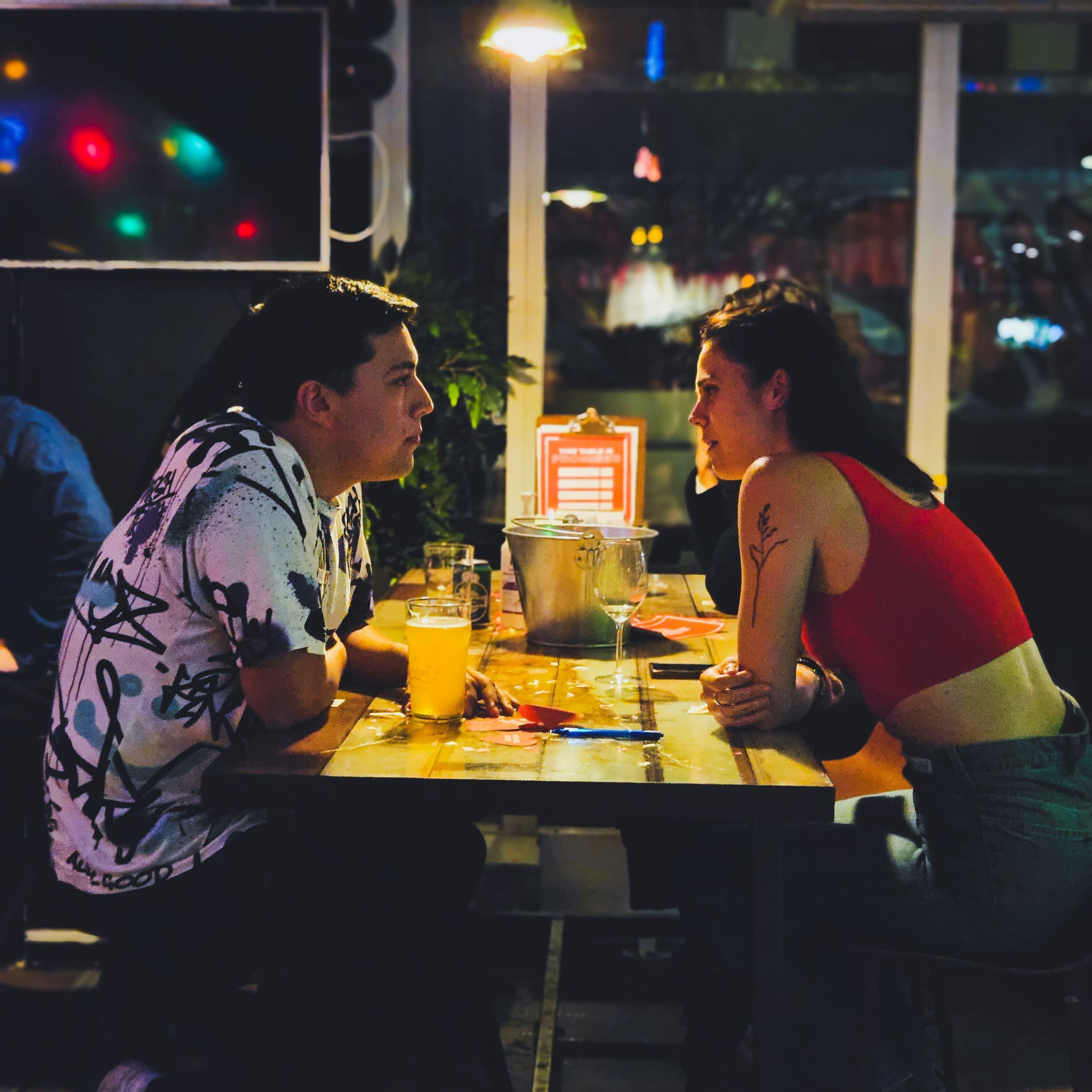 Duas pessoas sentadas à mesa com uma caneca de cerveja, uma garrafa e um cardápio.