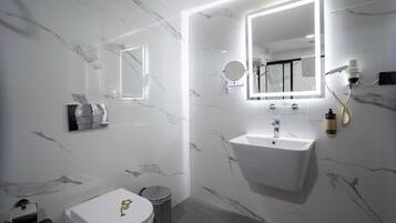 Um banheiro moderno com piso de mármore, pia branca com espelho acima e vaso sanitário com emblema dourado.