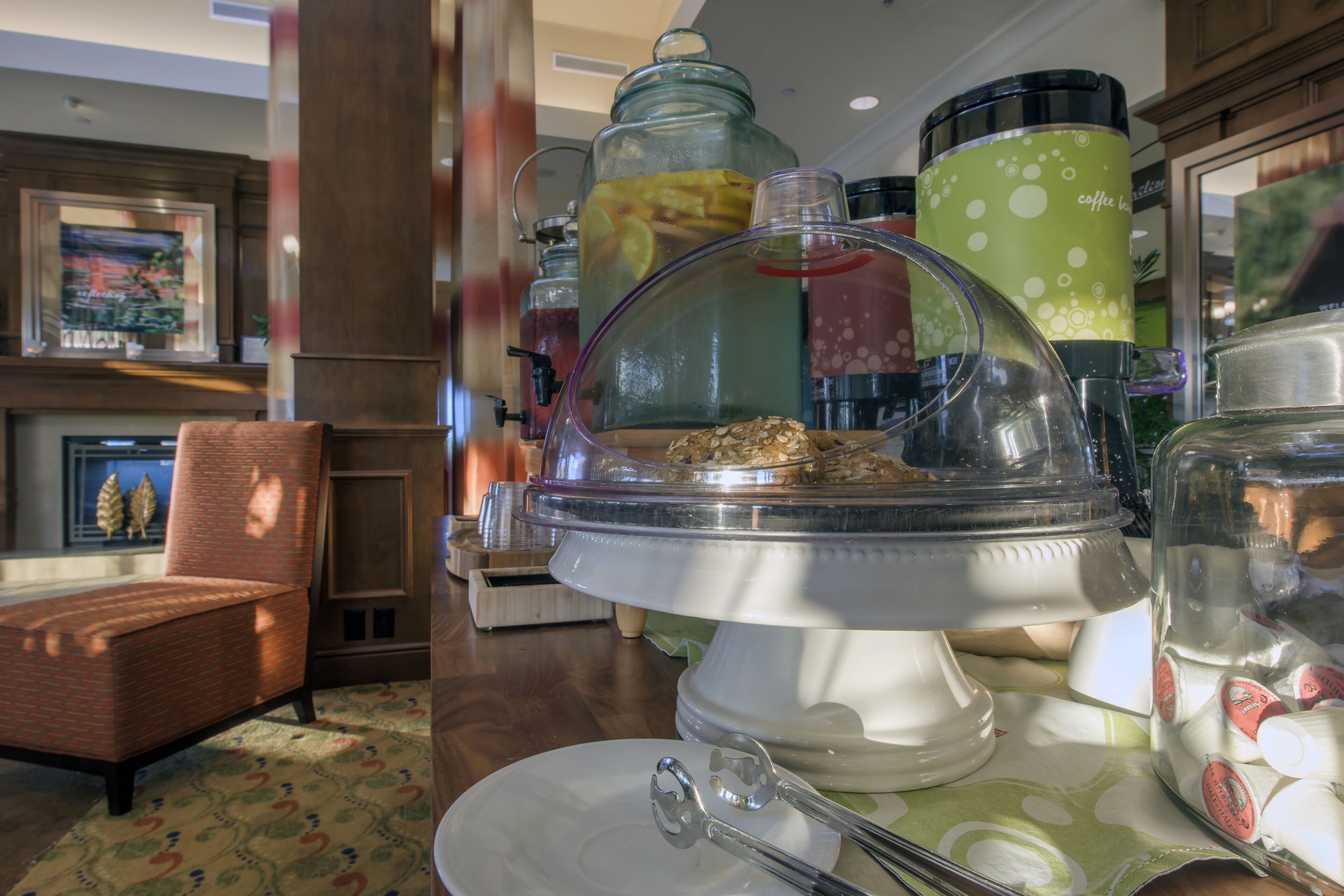 Espaço de buffet de café da manhã com diversas opções de comida e bebidas, uma cadeira e uma parede decorativa.