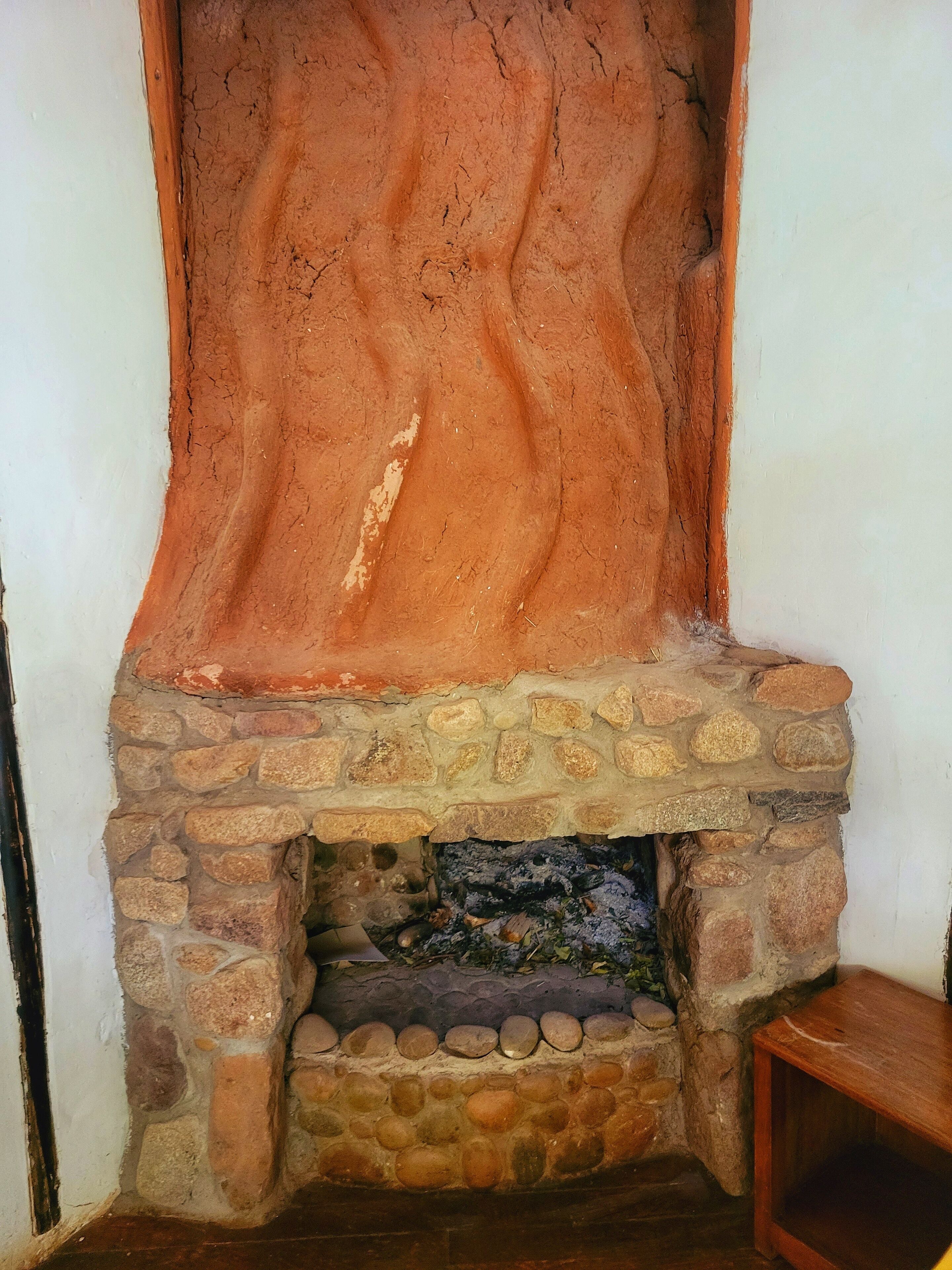 Lareira de pedra com aspecto rústico, destacando-se o rodapé de pedra e a abertura para a lenha.