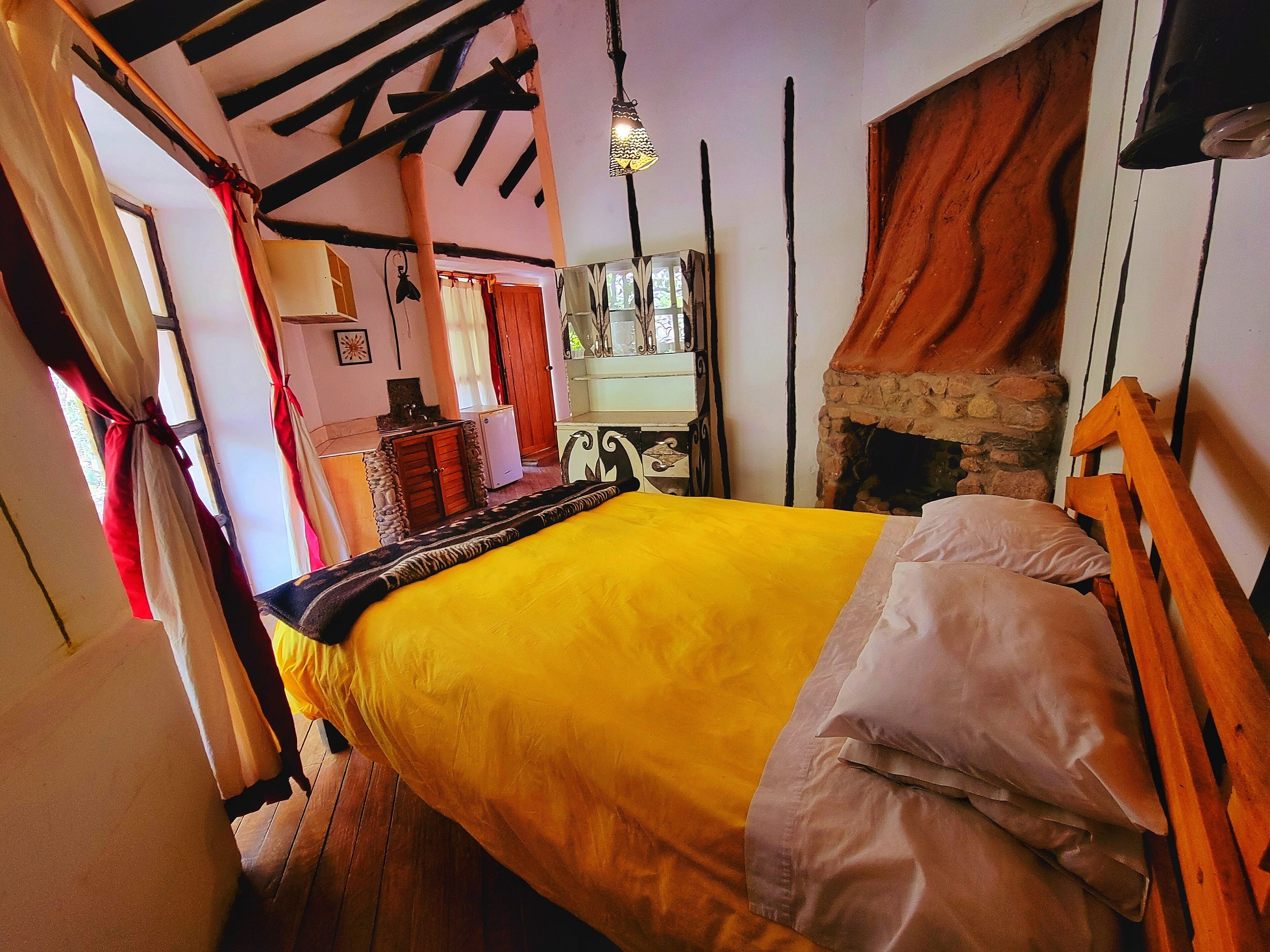 Quarto com cama, vigas de madeira, lareira de pedra e uma pequena mesa com um espelho.