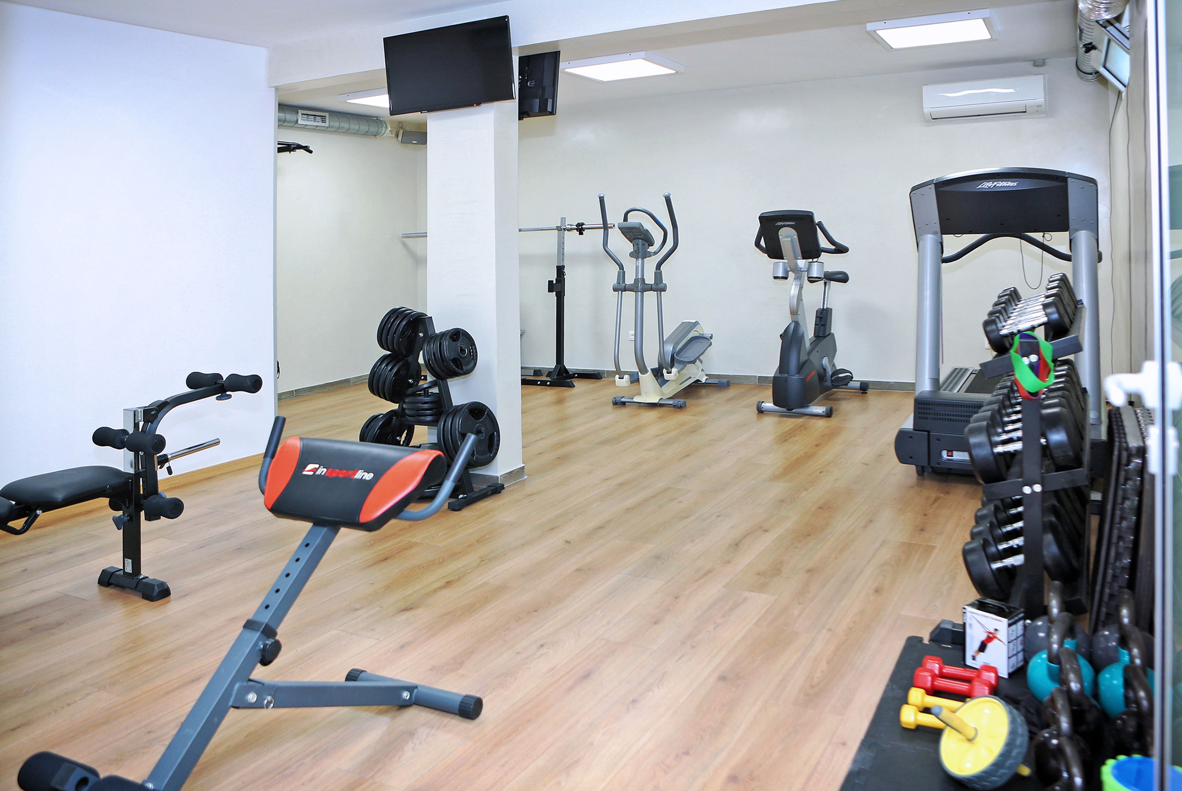 Uma academia com diversos equipamentos de exercícios, incluindo um banco, halteres, esteira e máquinas de peso.
