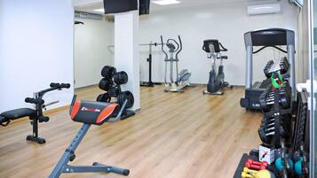 Uma academia com diversos equipamentos de exercícios, incluindo um banco, halteres, esteira e máquinas de peso.