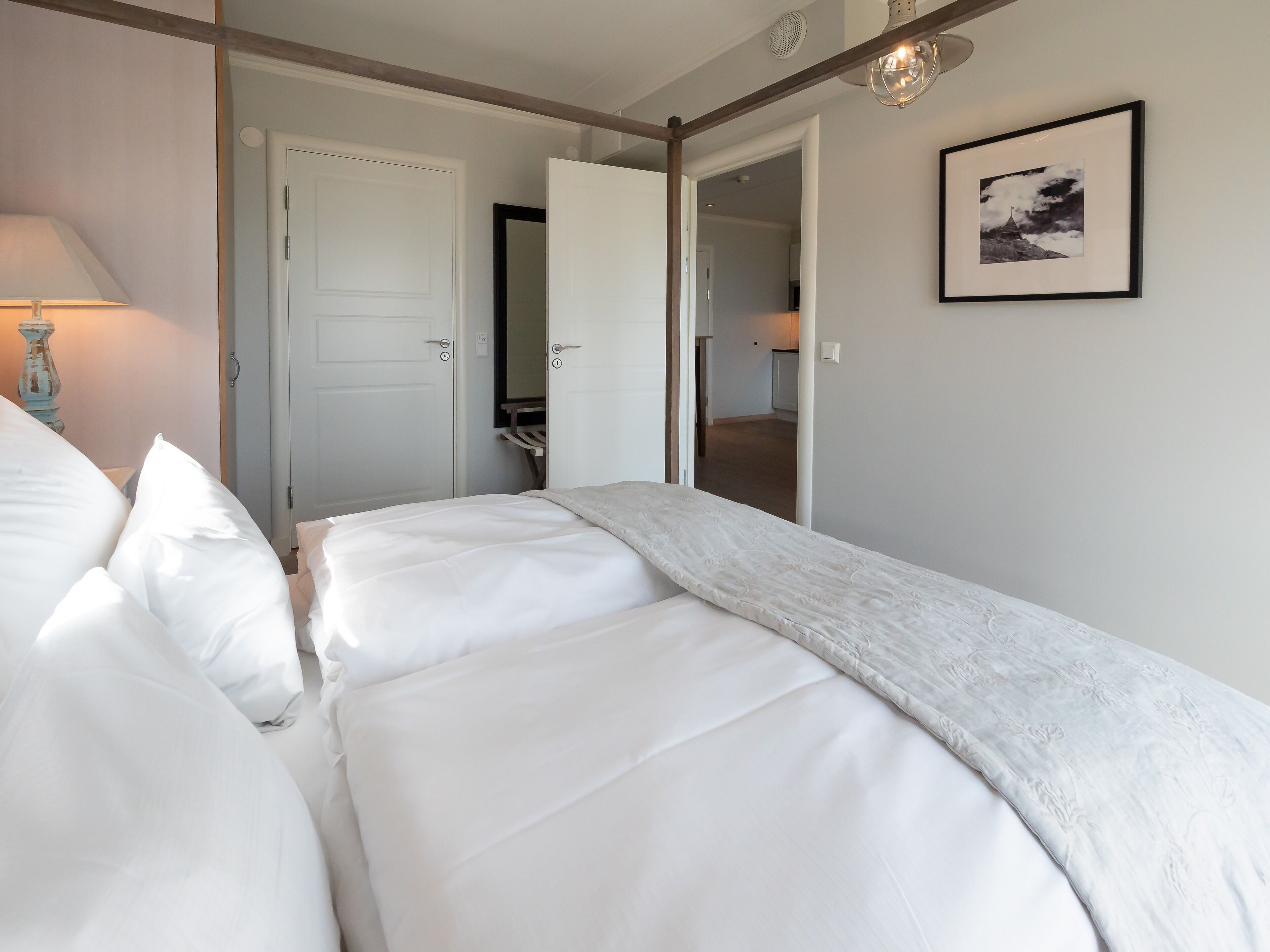 Quarto com cama, mesa de cabeceira, luminária, porta e um quadro na parede.