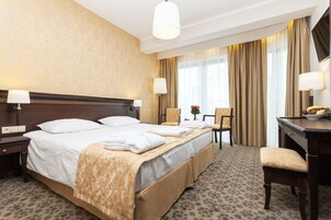 Quarto de hotel com uma cama grande, duas mesas de cabeceira, uma escrivaninha e uma cadeira.
