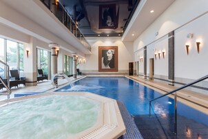 Uma grande piscina interna com hidromassagem, espreguiçadeiras e um mural na parede.