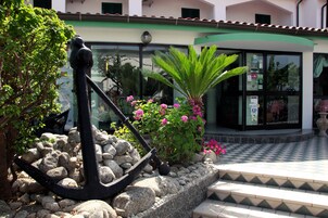 Um edifício com entrada em azulejos, uma parede de pedra com decoração de âncora e uma planta de palmeira.