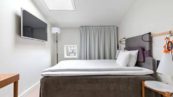Quarto de hotel moderno com uma cama grande, televisão de tela plana na parede, mesa de cabeceira, abajur e suporte para bicicleta.