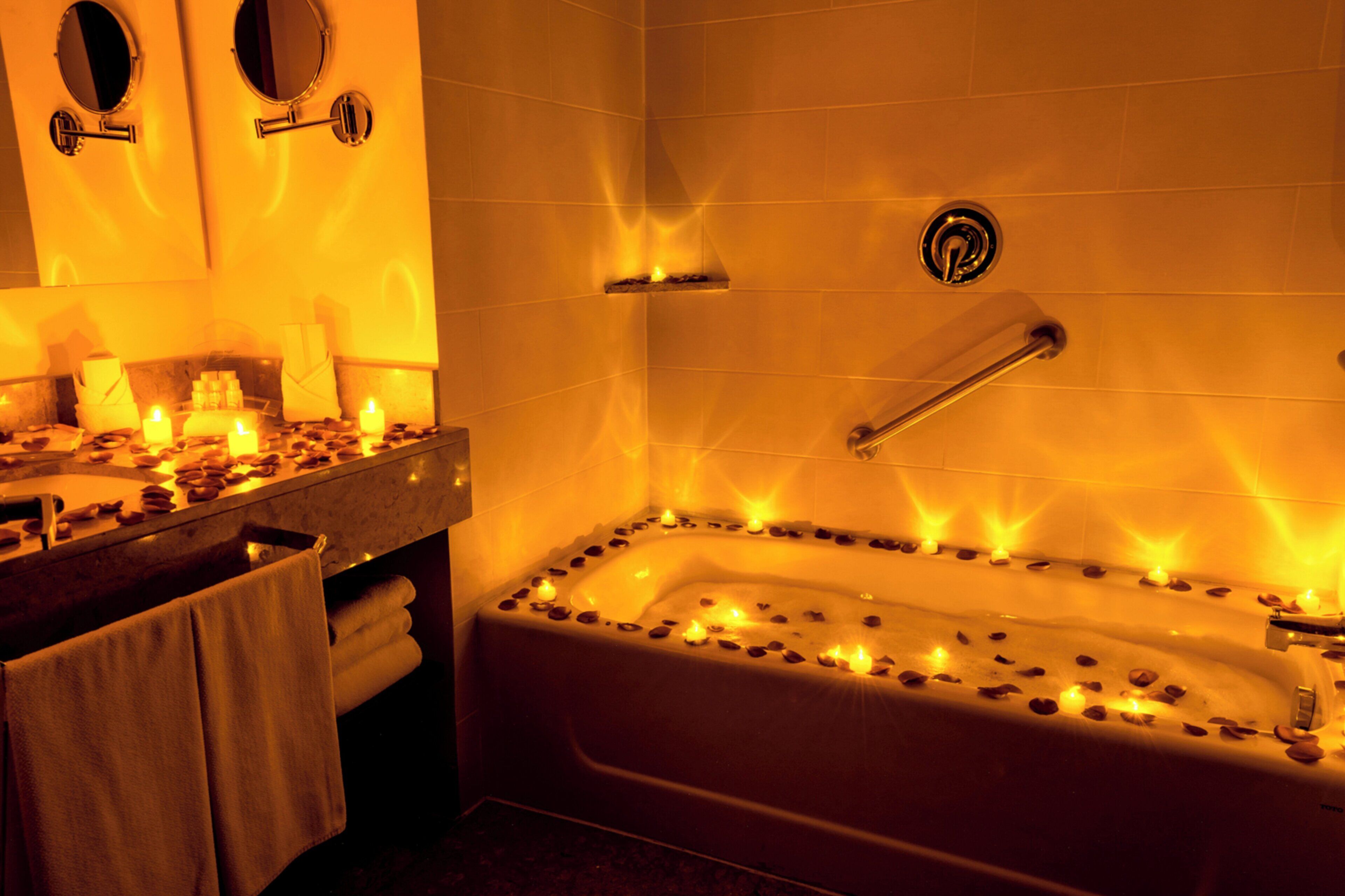 Um banheiro com banheira cercada por velas, espelho e porta-toalhas.
