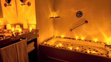 Um banheiro com banheira cercada por velas, espelho e porta-toalhas.