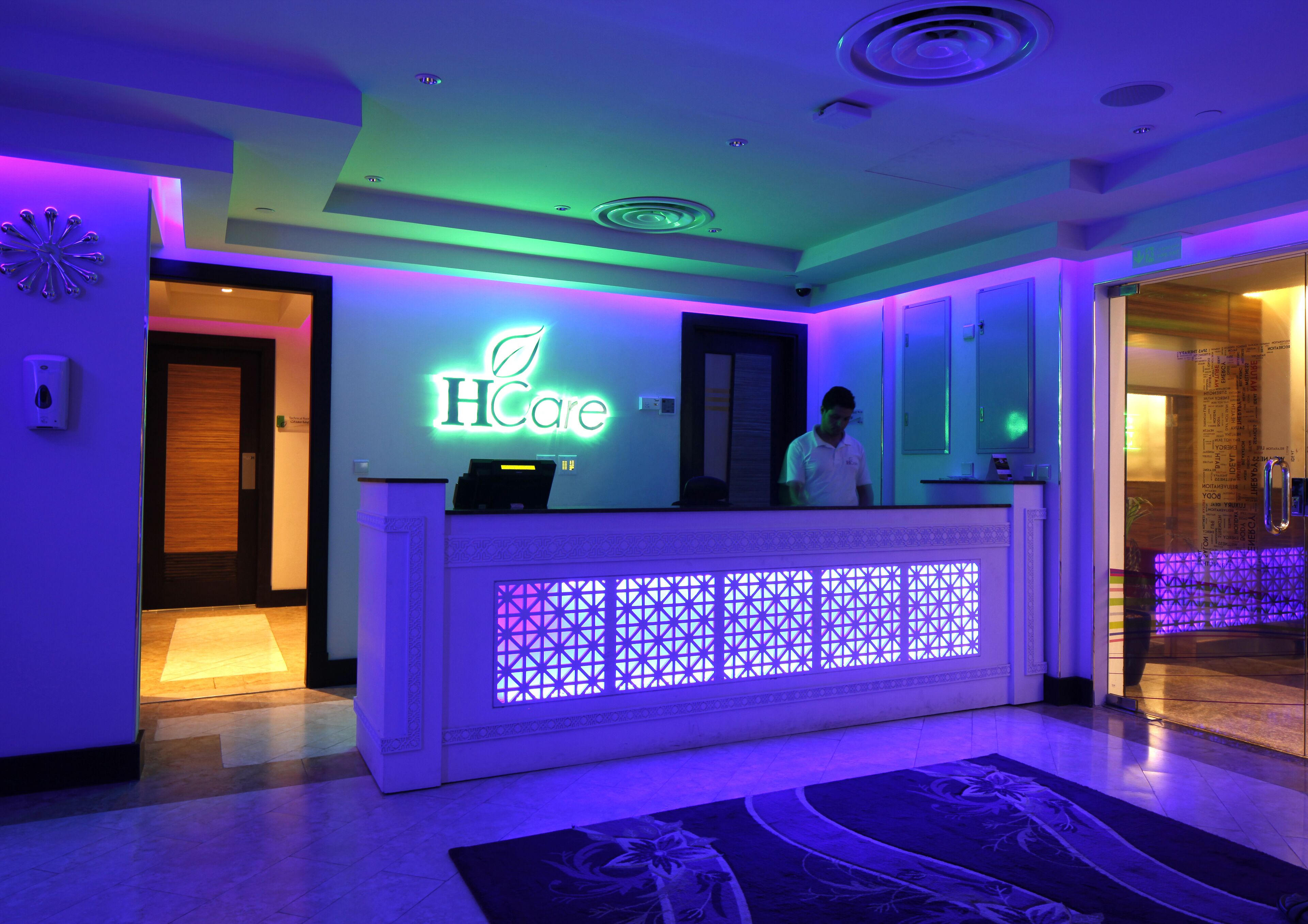Uma mesa de recepção com um letreiro de neon que diz "HCare" e uma divisória de vidro com padrão.