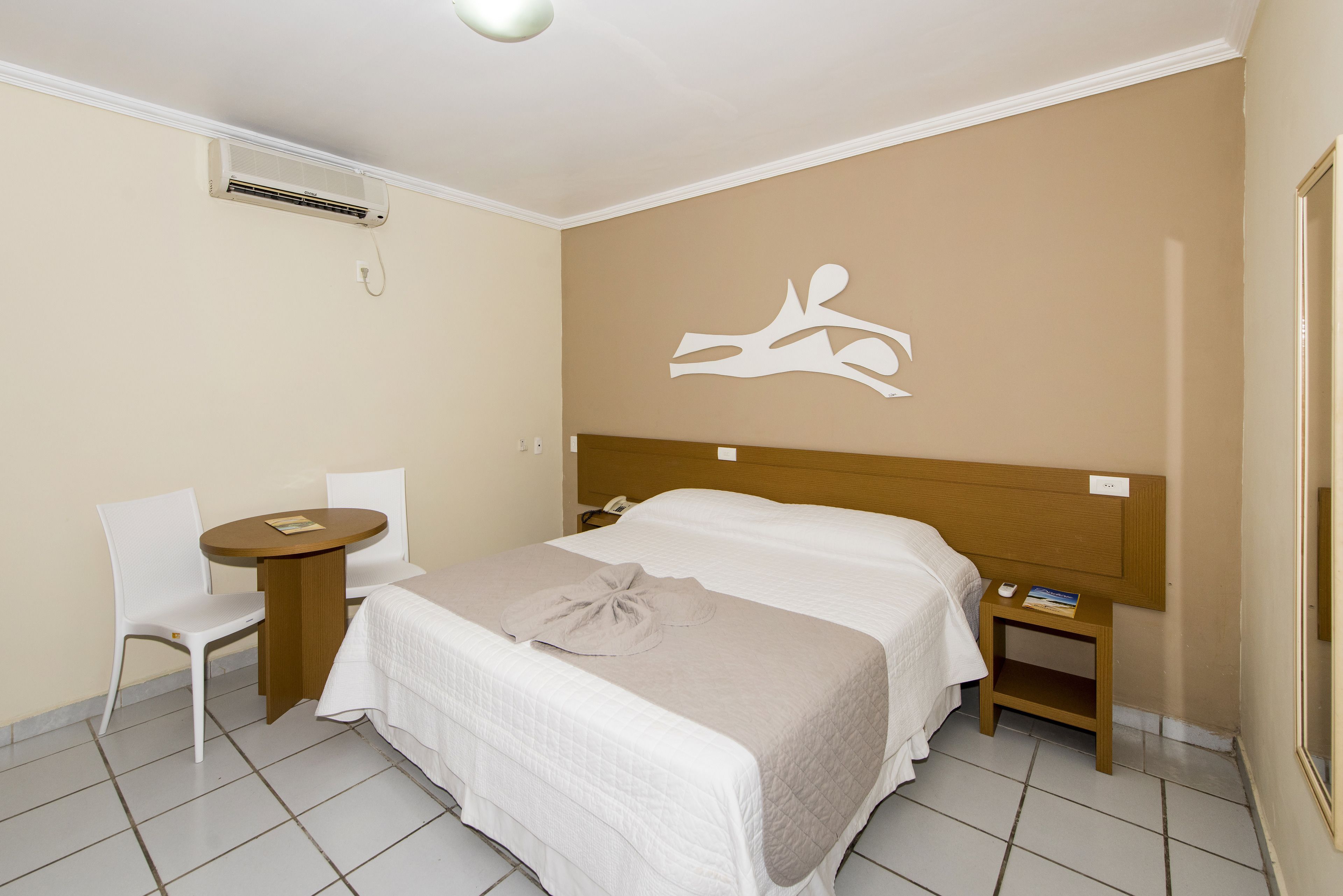 Quarto de hotel com cama, mesa de cabeceira, cadeira e ar condicionado fixado na parede.