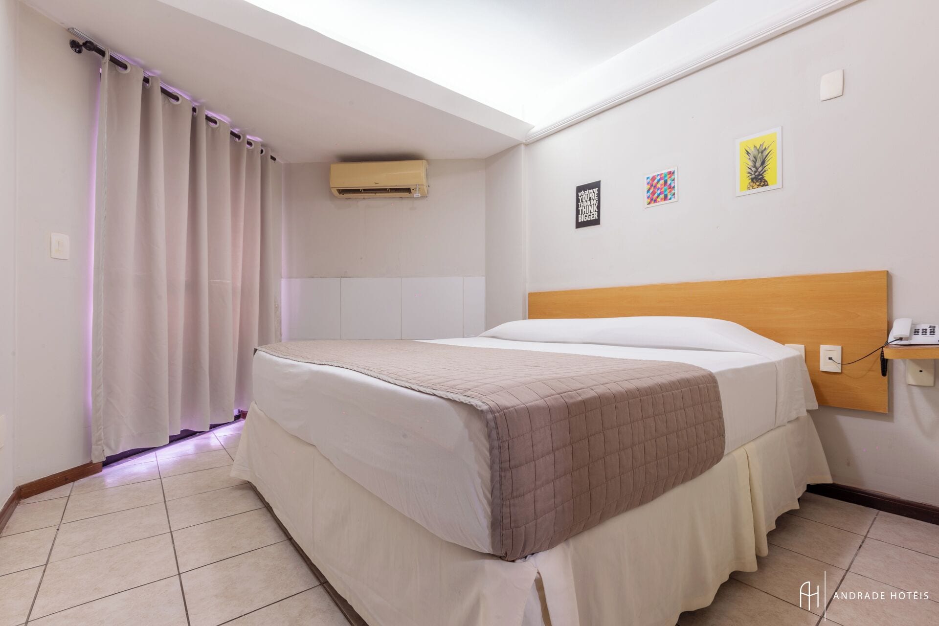 Quarto de hotel com cama, cortinas, aparelho de ar condicionado e obras de arte nas paredes.