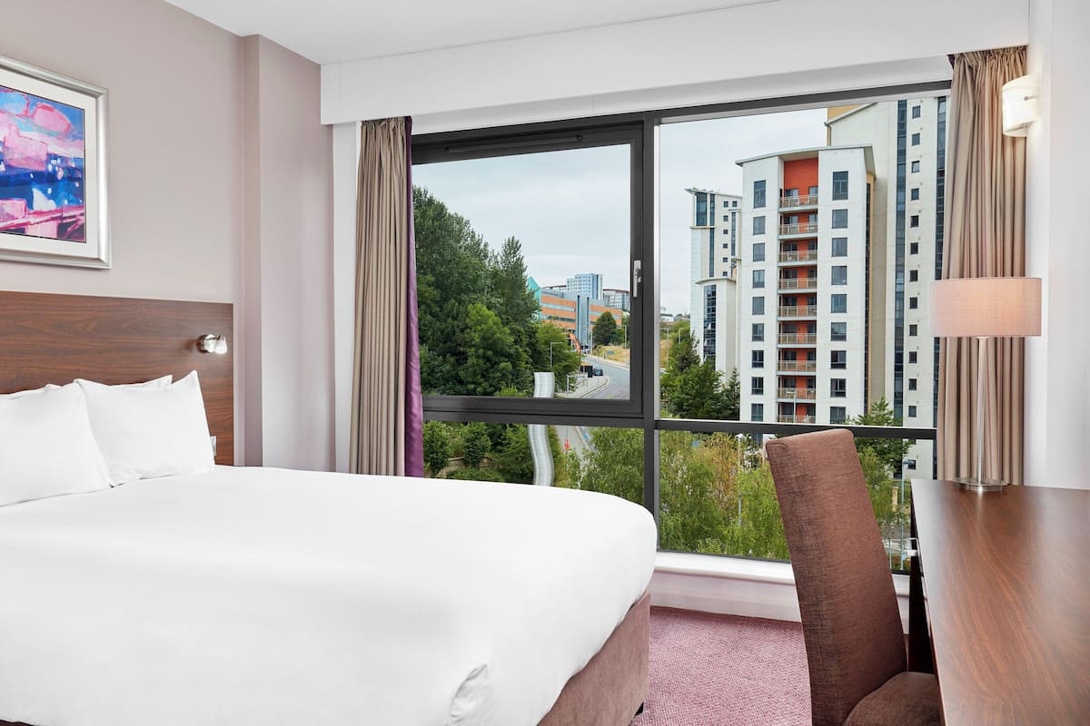 Quarto de hotel com uma cama grande, uma escrivaninha e vista para edifícios altos.