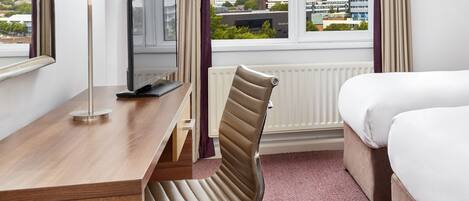 Quarto de hotel com escrivaninha de madeira, uma cadeira moderna, uma cama e vista para a cidade pela janela.