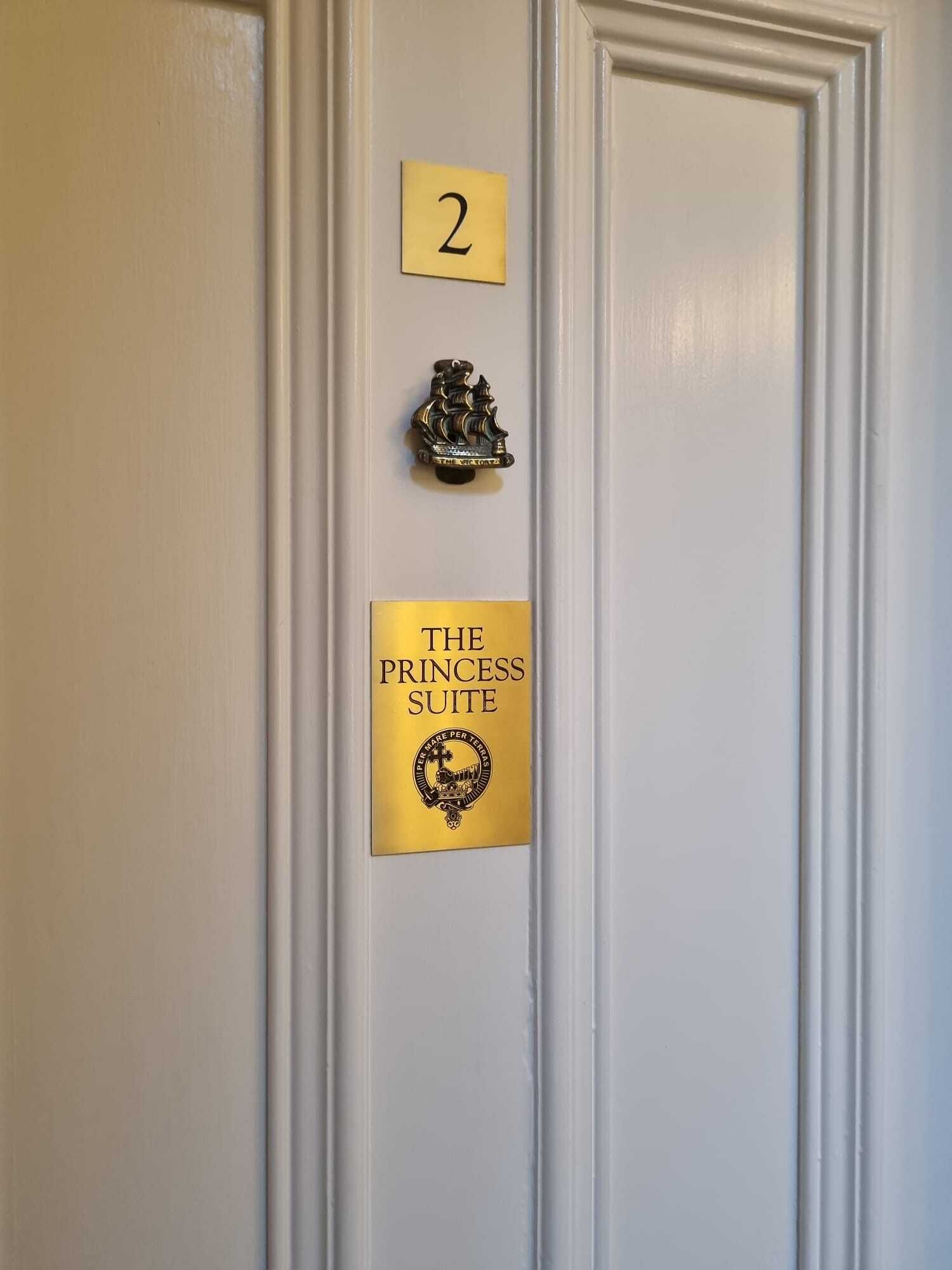 Uma porta com um espelho de latão e uma placa dourada com a inscrição 'THE PRINCESS SUITE'.