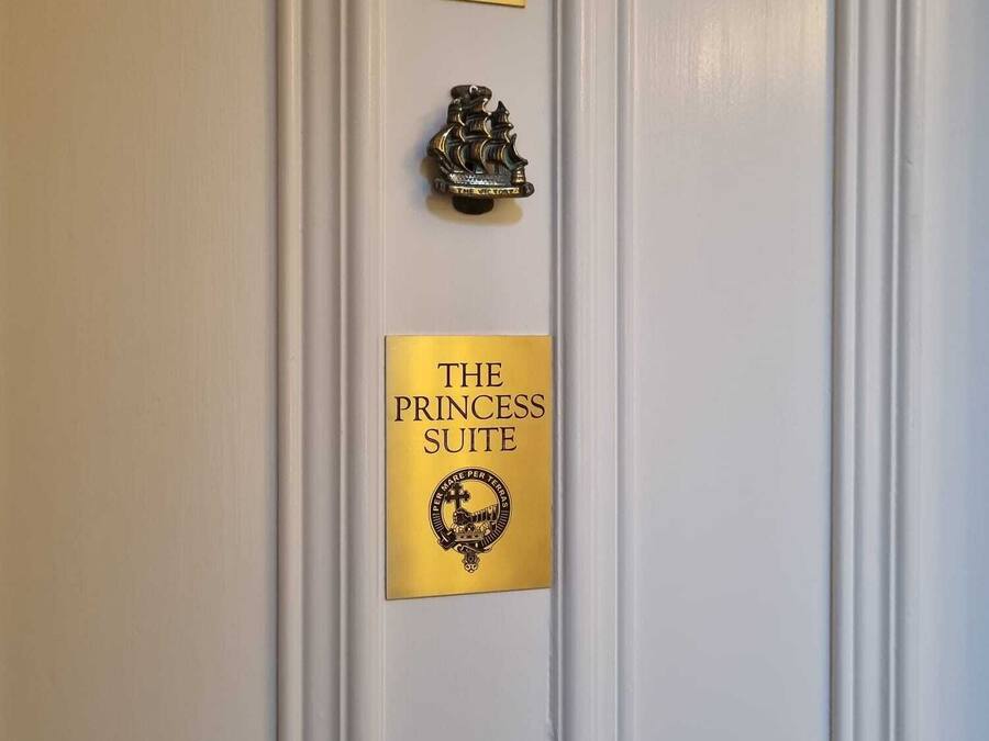 Uma porta com um espelho de latão e uma placa dourada com a inscrição 'THE PRINCESS SUITE'.